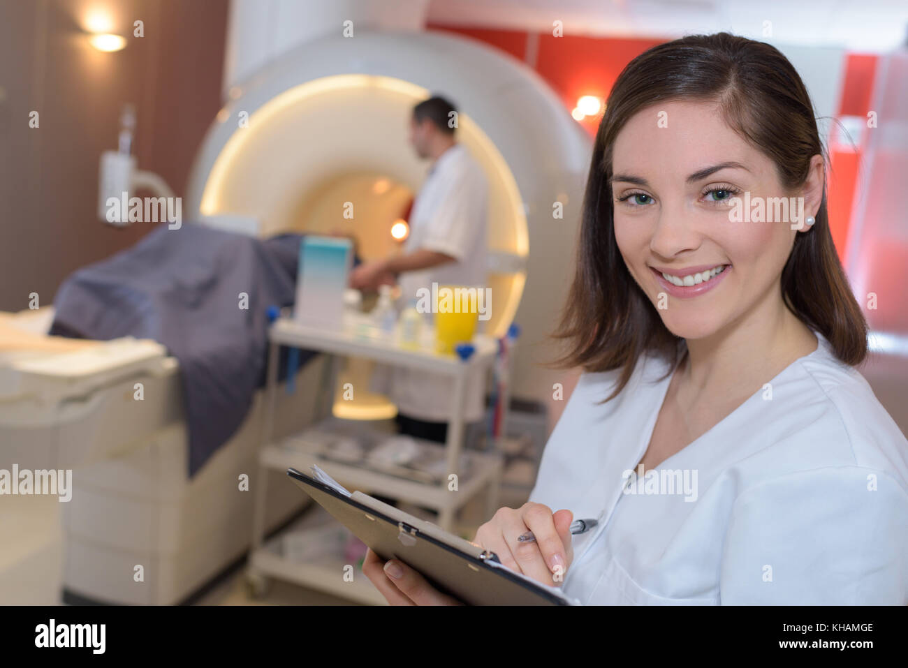 happy female radiologist with colleagues in background by mri machine ...
