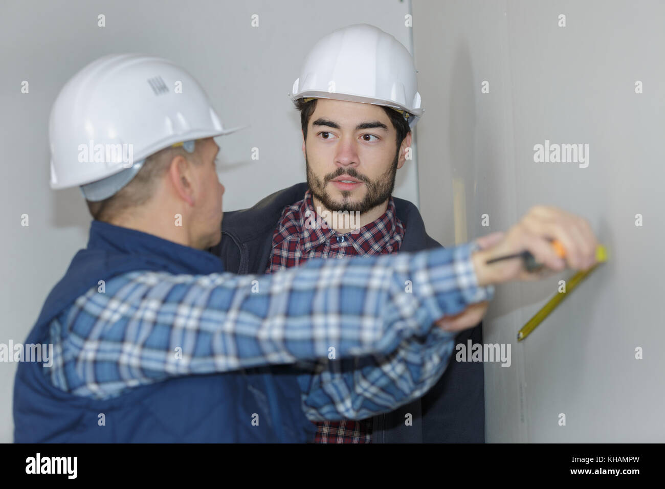 two workmen measuring interior wall with tae measure Stock Photo - Alamy