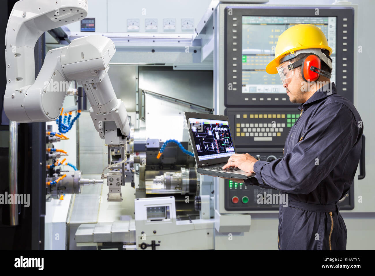 Maintenance engineer using laptop computer control automatic robotic hand with CNC machine in ...