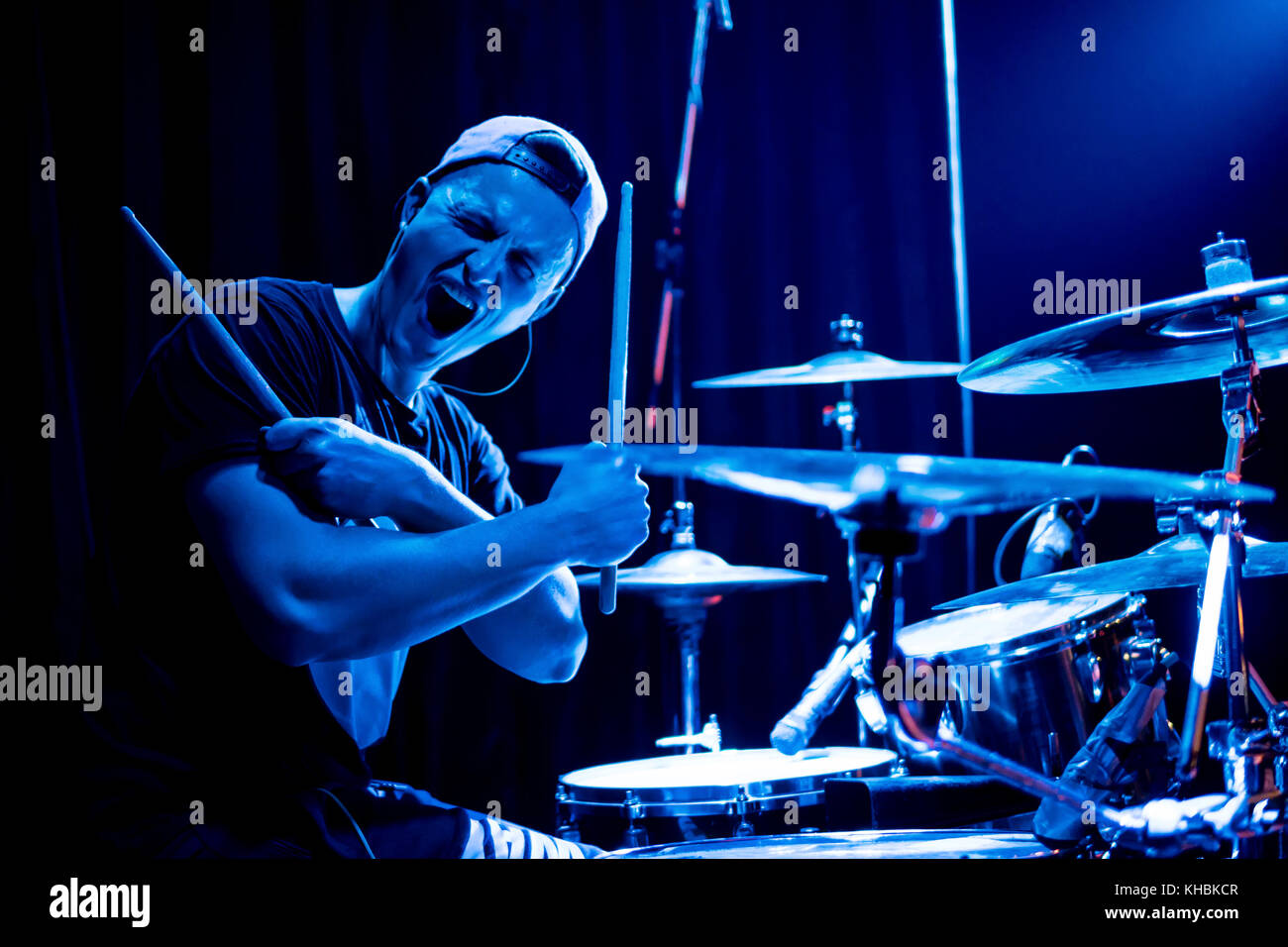 Young drummer posing in front of the camera in a blue concert light ...