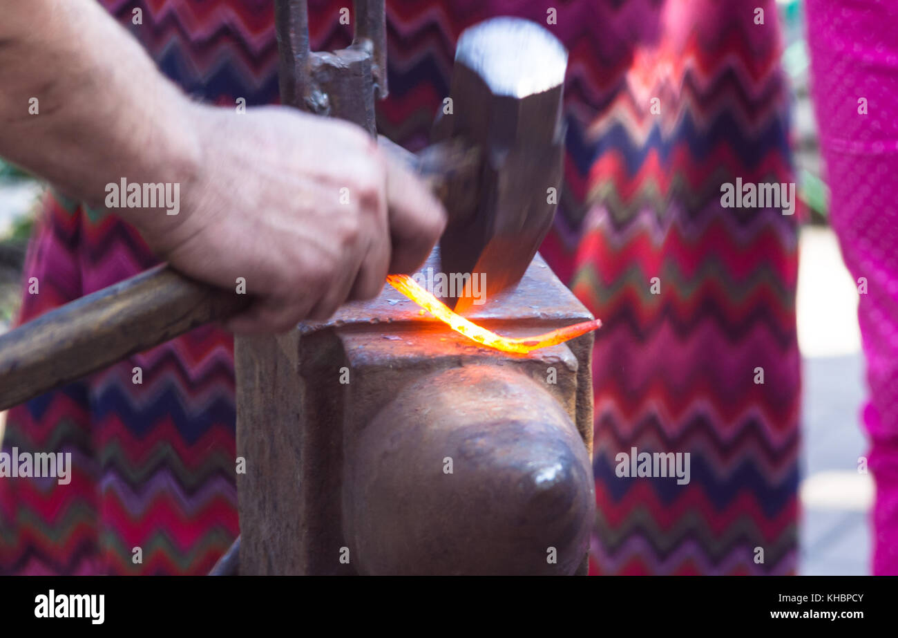 blacksmith performs the forging of hot glowing metal on the anvil ...