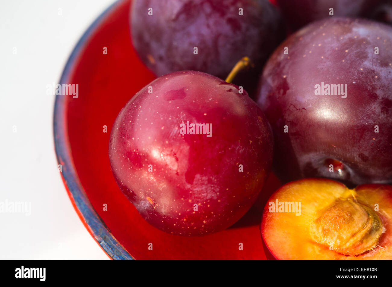 fresh plum fruit with cut plum slices in the red saucer on white ...