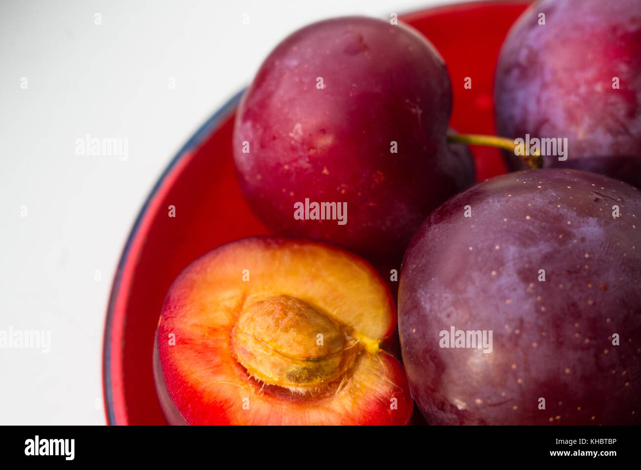 fresh plum fruit with cut plum slices in the red saucer on white ...