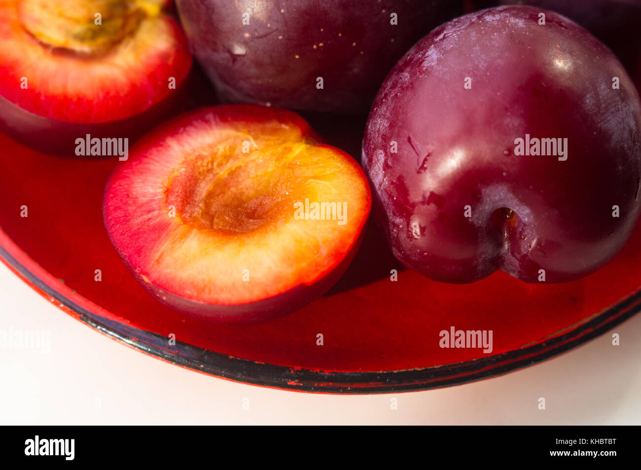 fresh plum fruit with cut plum slices in the red saucer on white ...