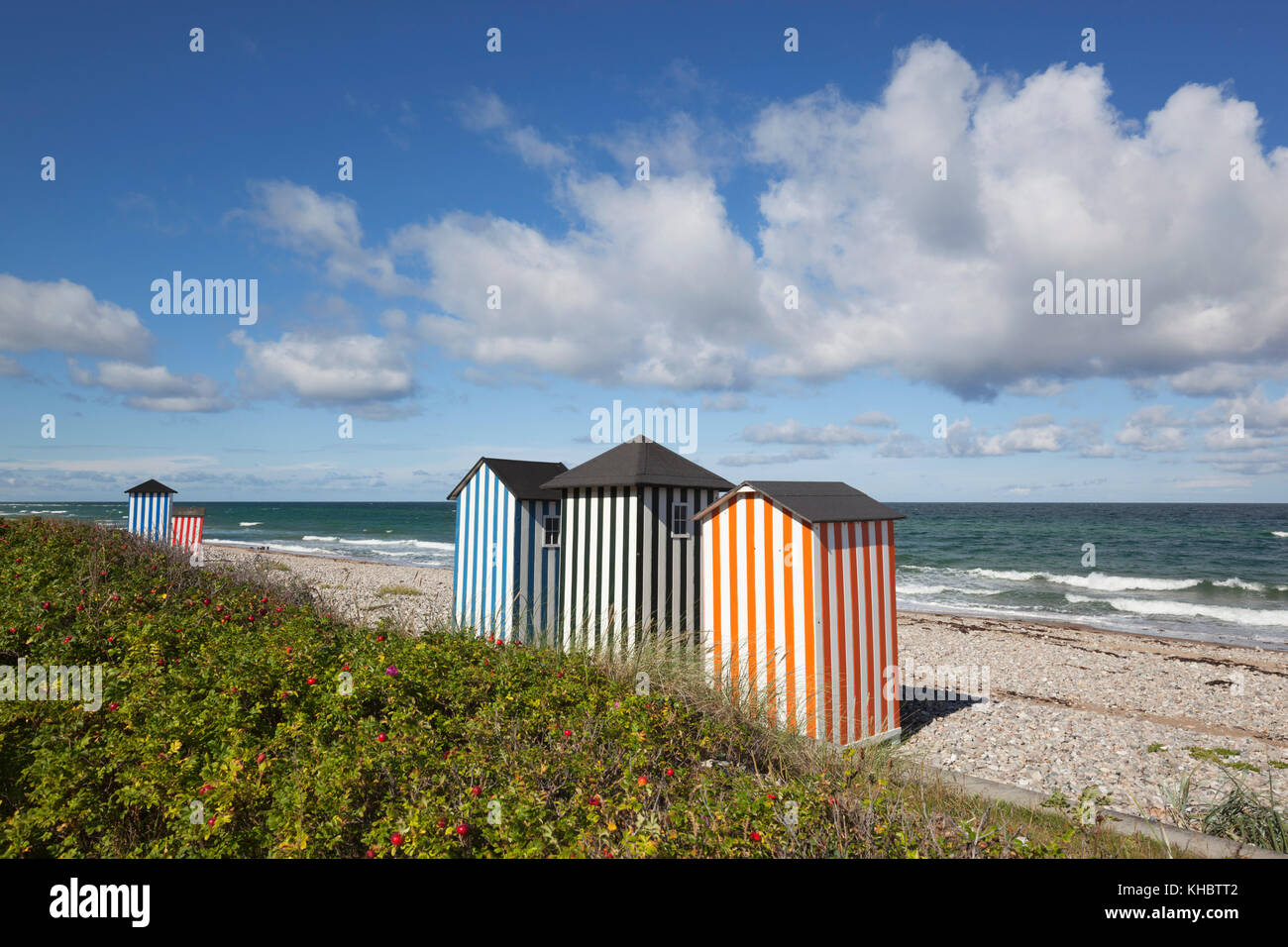 Colourful beach huts on pebble beach with blue sea and sky with clouds ...