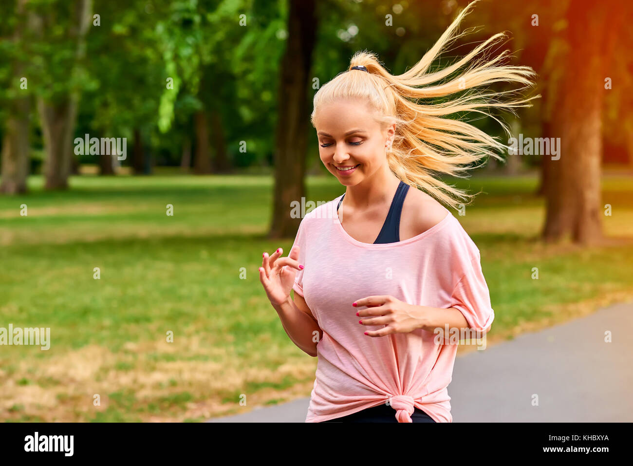 Portrait of a beautiful young blonde woman while running in a park ...
