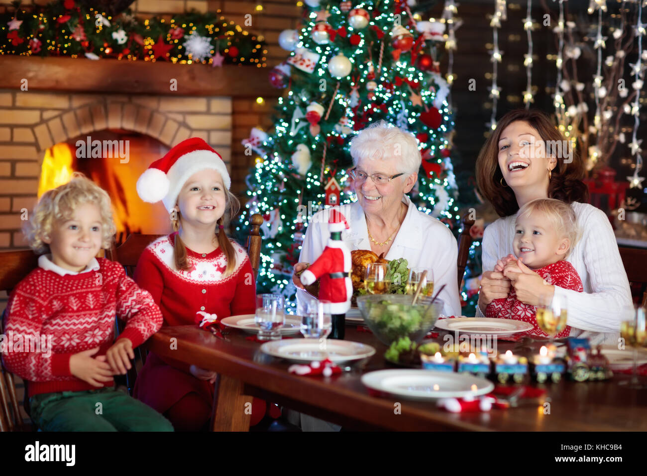 Family with children eating Christmas dinner at fireplace and decorated ...