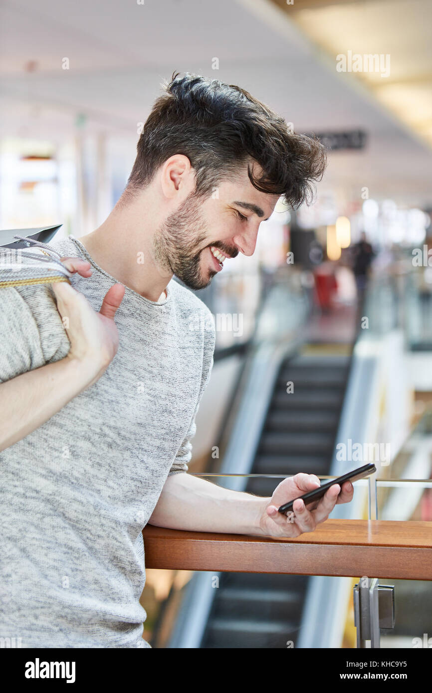 Happy young man with smartphone while shopping in shopping mall Stock ...