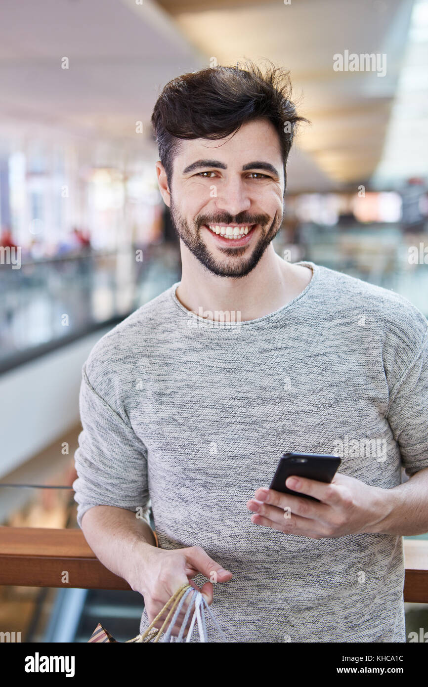 Happy young man with smartphone while shopping in shopping mall Stock ...