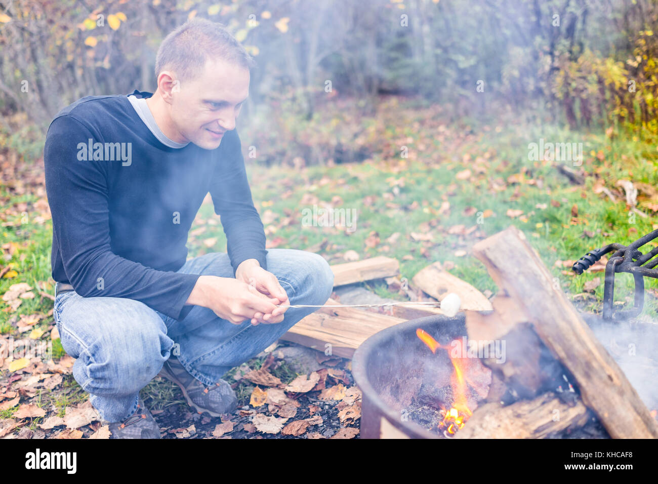 Closeup of young happy smiling man roasting one white marshmallow ...