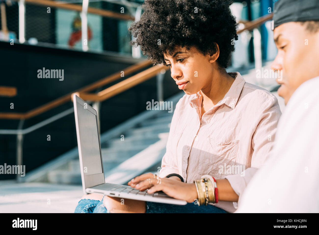 Young multiethnic couple using computer sitting outdoor in the city ...
