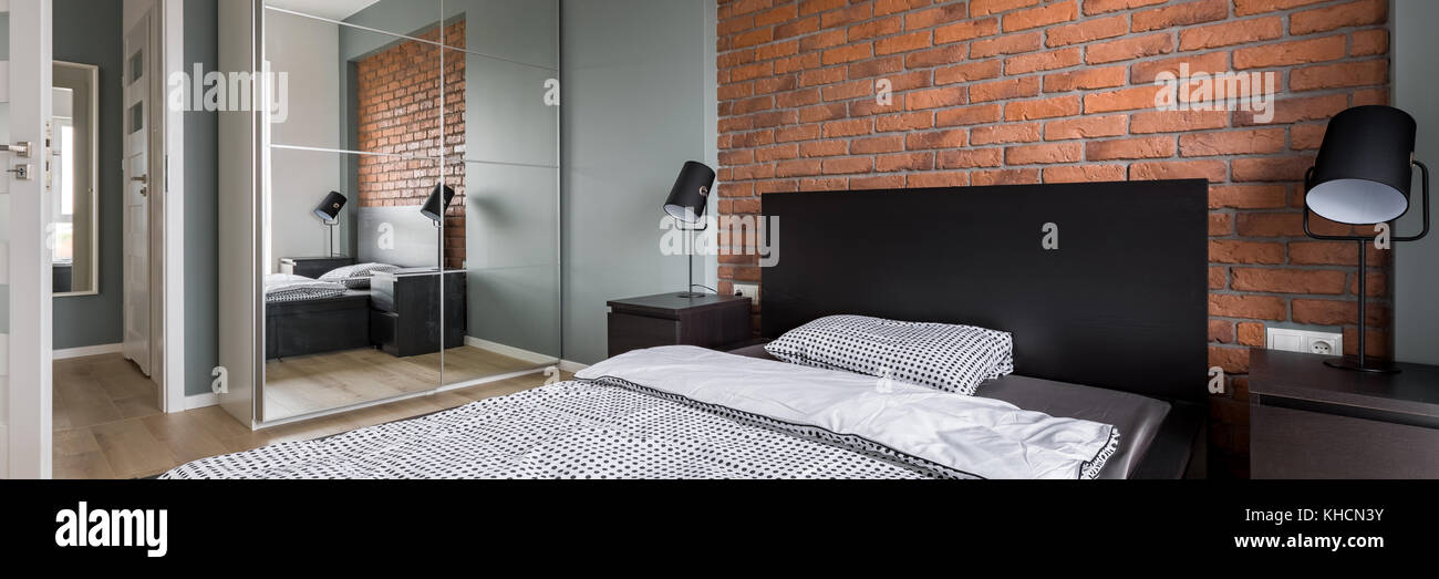 Panorama of modern bedroom with brick wall, mirrored wardrobe and bed ...