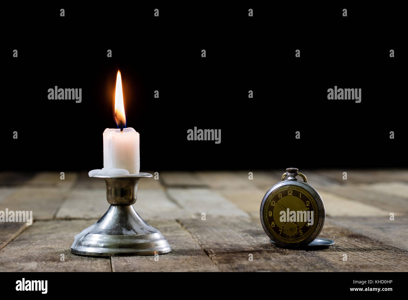 Burning candle and old watch on a wooden table. Flowing time and ...