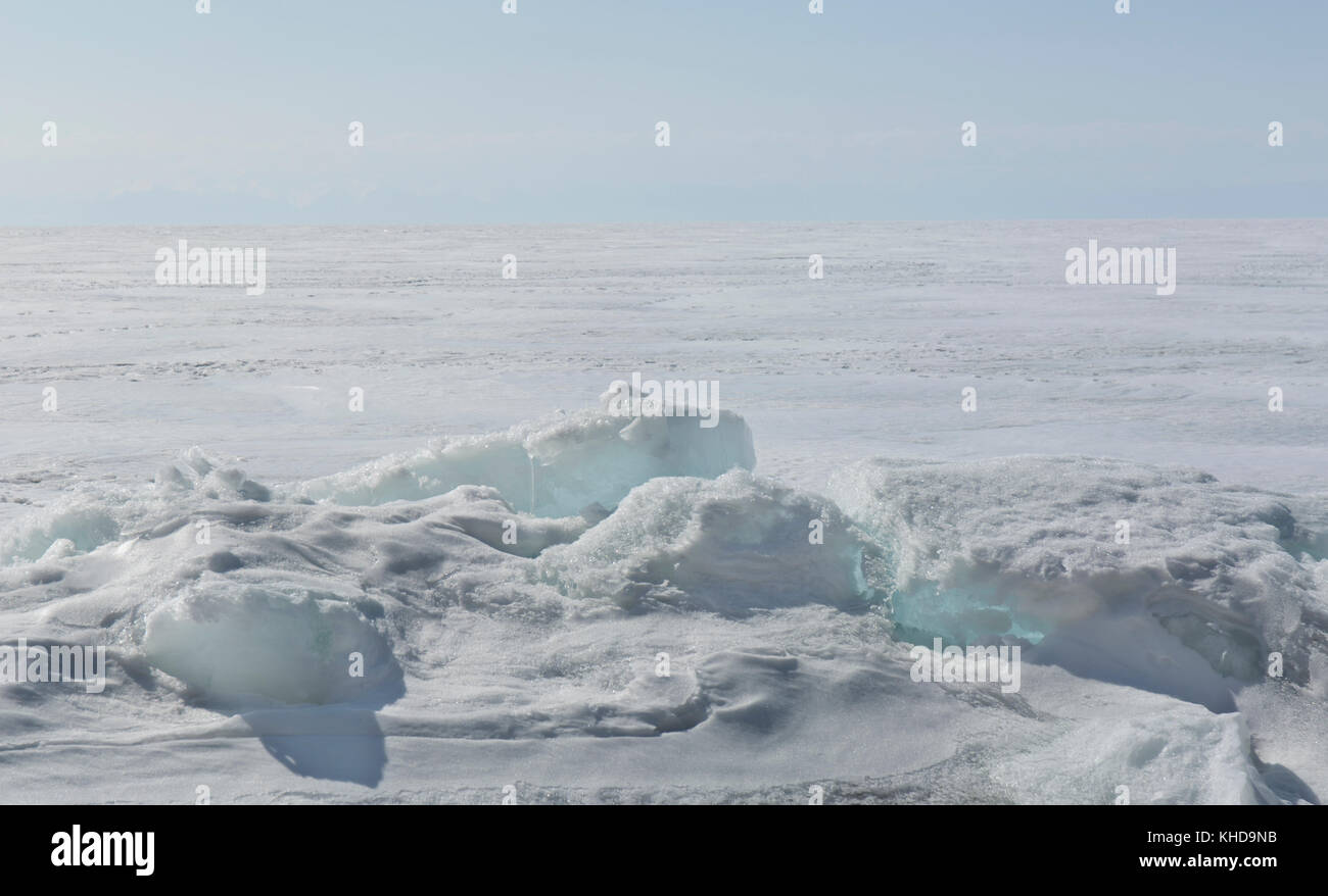Transparent blue ice hummocks on lake Baikal shore. Siberia winter landscape view. Snow-covered ...