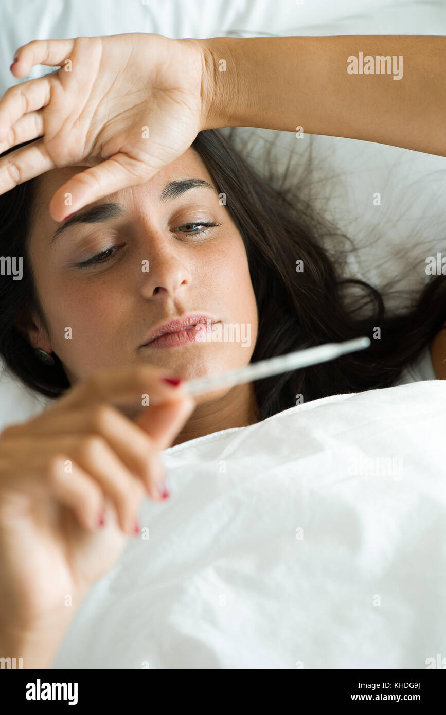 Woman lying in bed taking temperature with thermometer Stock Photo - Alamy