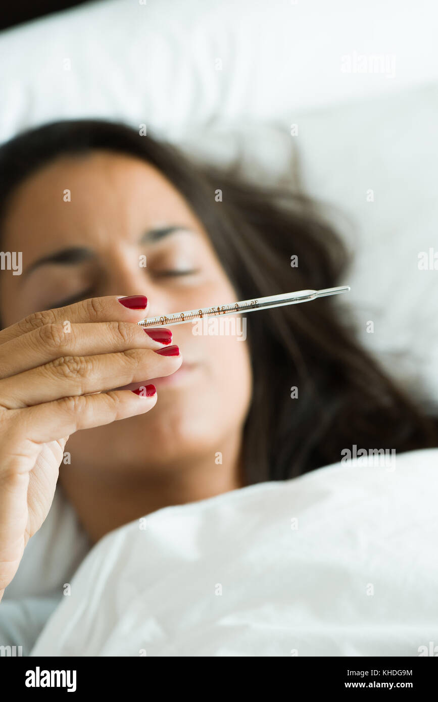 Woman lying in bed taking temperature with thermometer Stock Photo - Alamy
