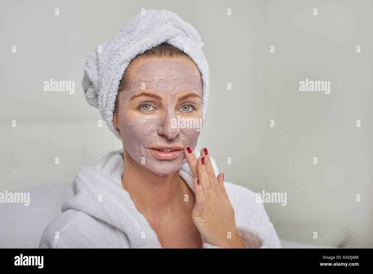 Attractive woman in a white towelling robe applying a face mask while ...
