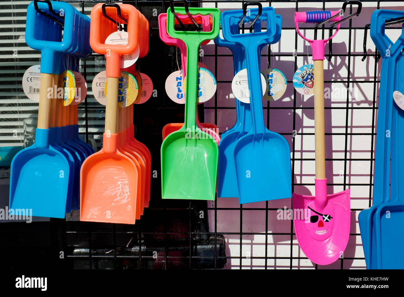 Brightly coloured plastic toy spades hanging on display outside a shop ...