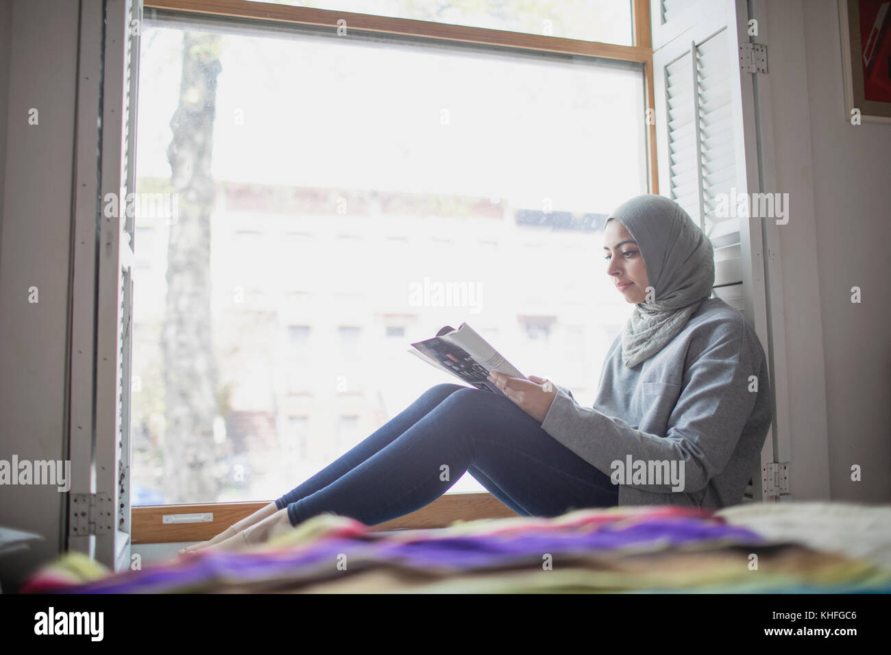 Muslim woman wearing a hijab reading on a window sill Stock Photo - Alamy
