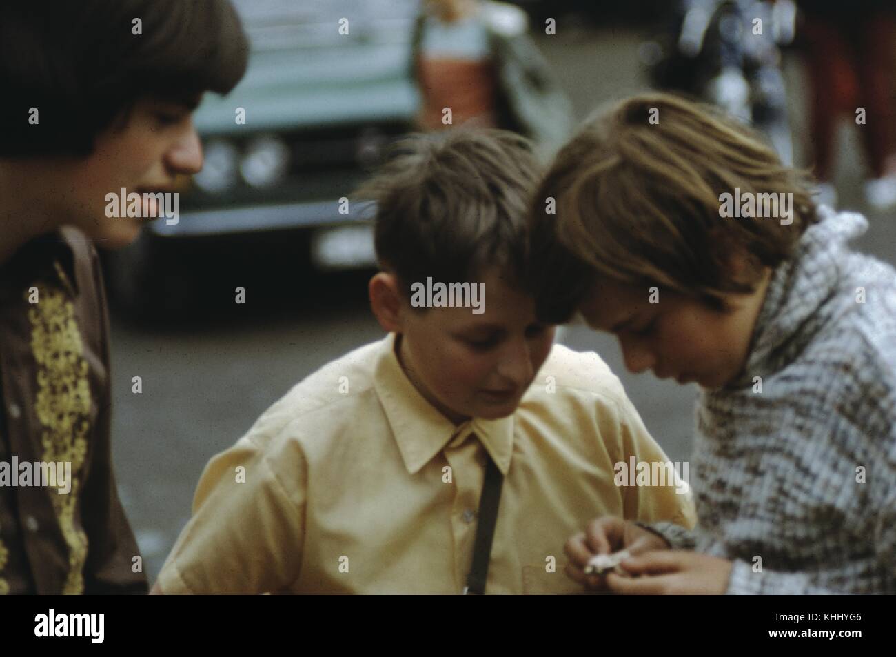 A photograph of three teenage boys examining an object that is obscured ...