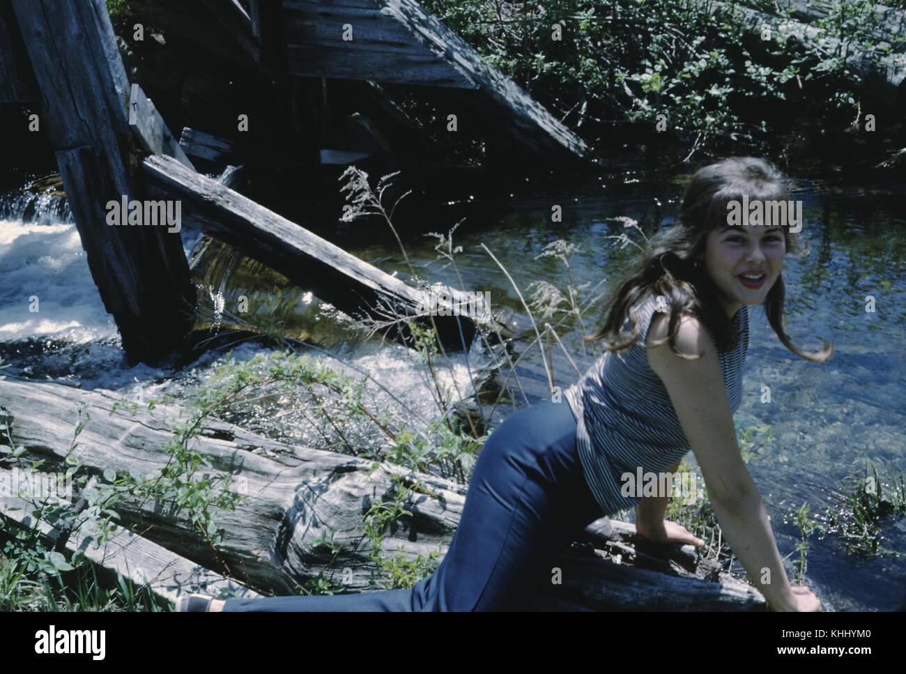Woman wearing jeans and a red bandanna climbing over a log towards a ...
