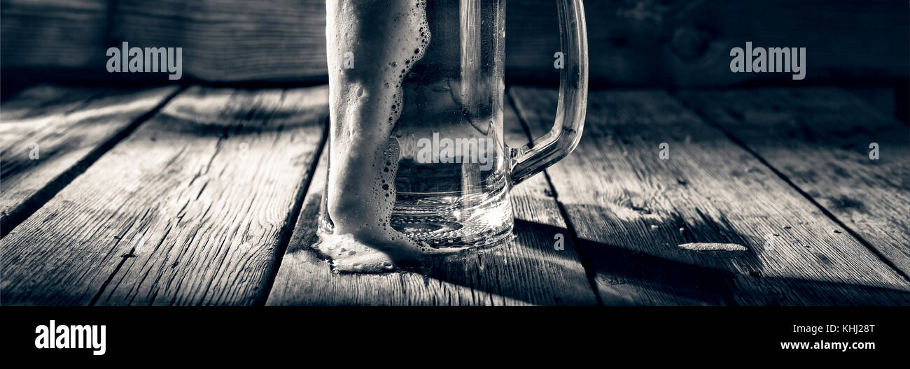 Black and white. Mug of light beer pills with foam on a wooden table in ...