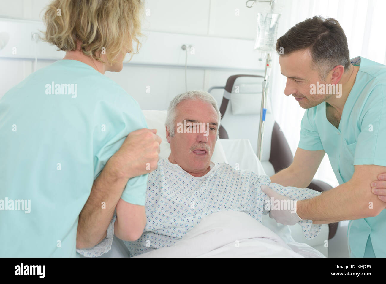 older man lying in hospital bed with nurses helping him Stock Photo - Alamy
