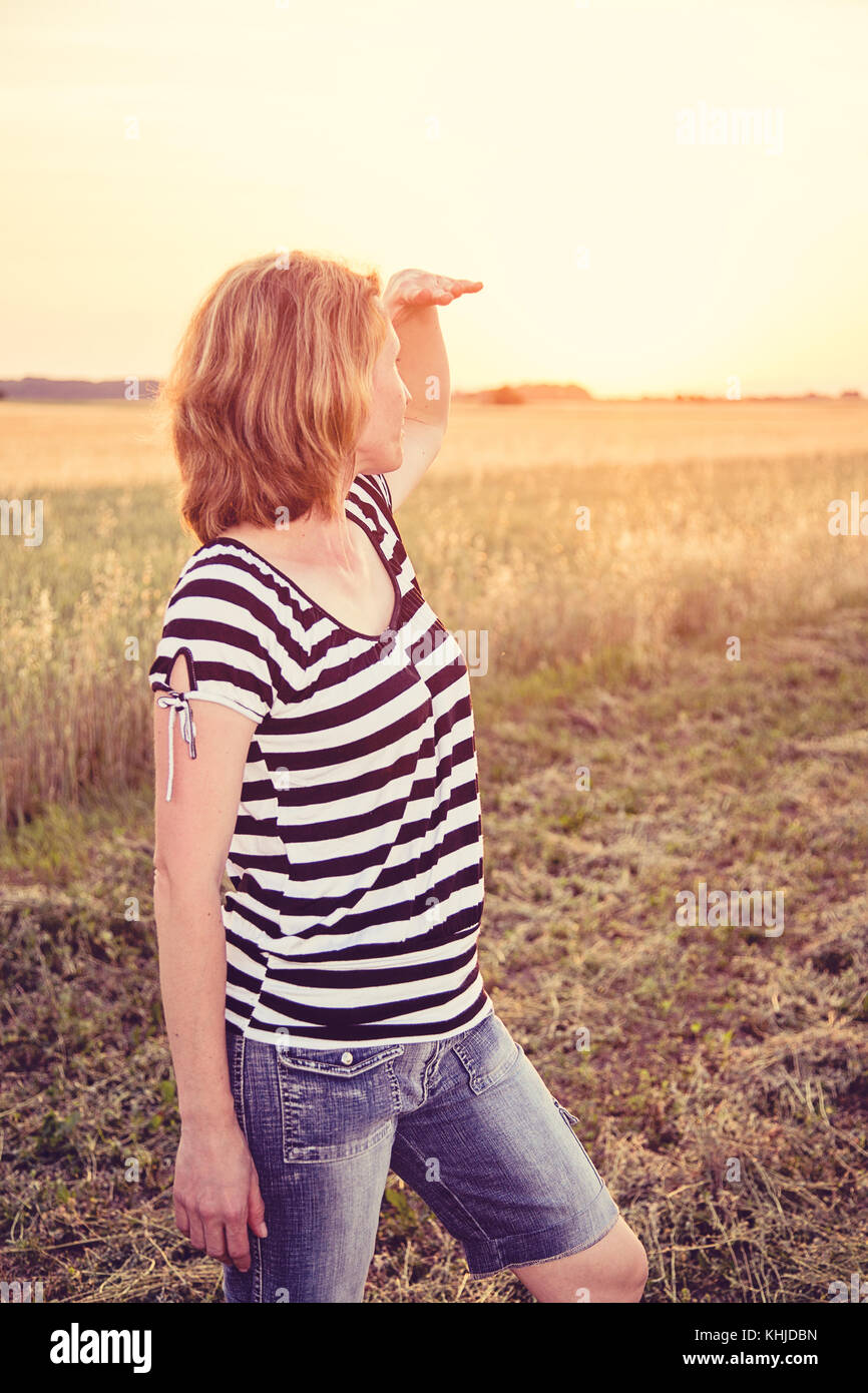 Young caucasian woman looking into distance at sunset. She is standing ...