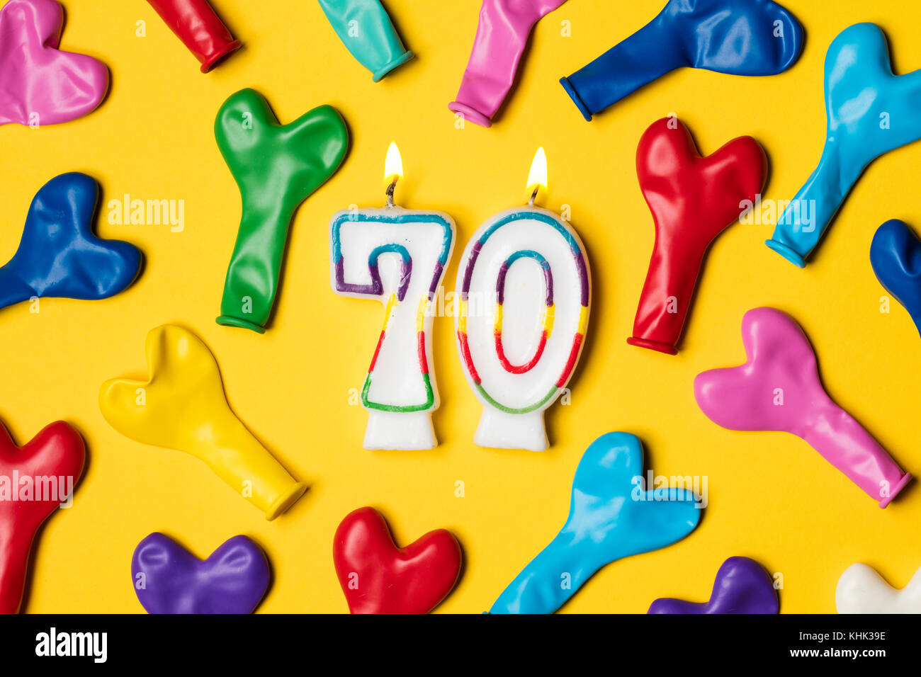 Number 70 candle with party balloons on a bright yellow background ...