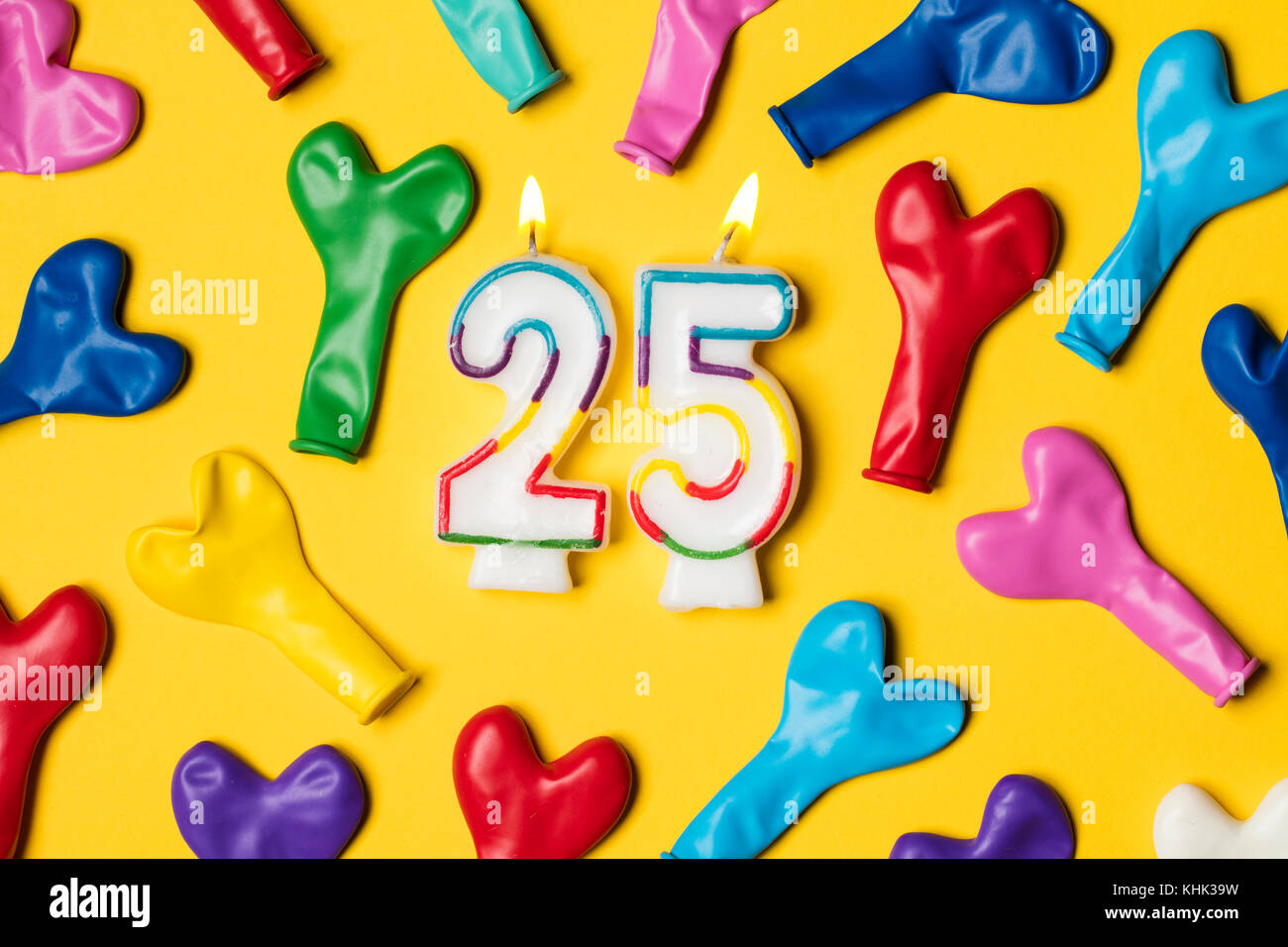 Number 25 candle with party balloons on a bright yellow background ...