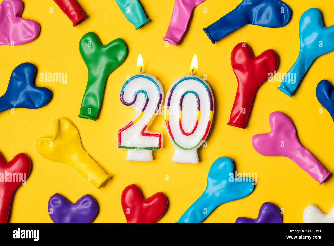 Number 20 candle with party balloons on a bright yellow background ...