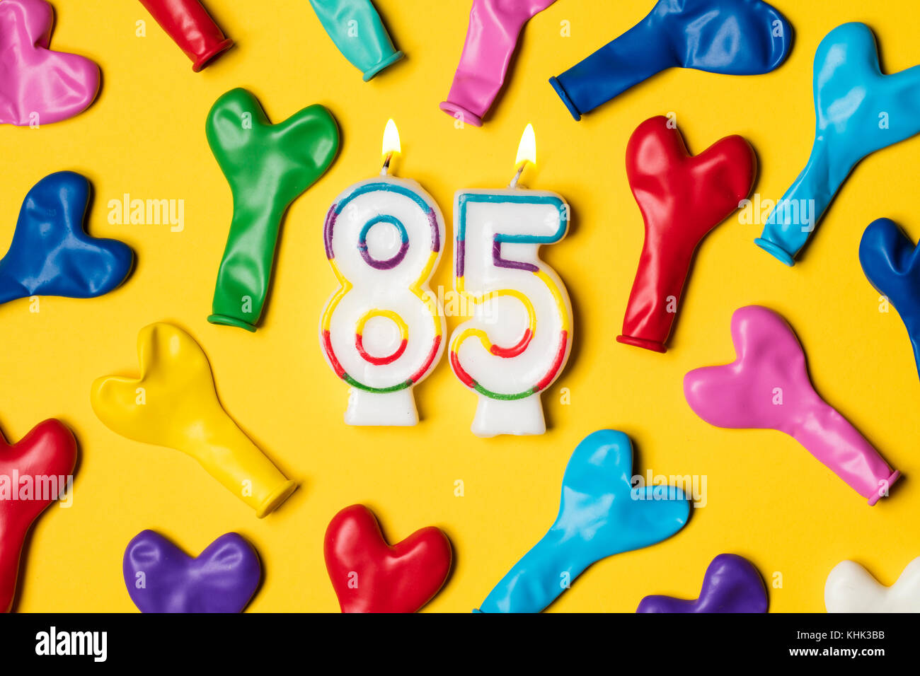 Number 85 candle with party balloons on a bright yellow background ...
