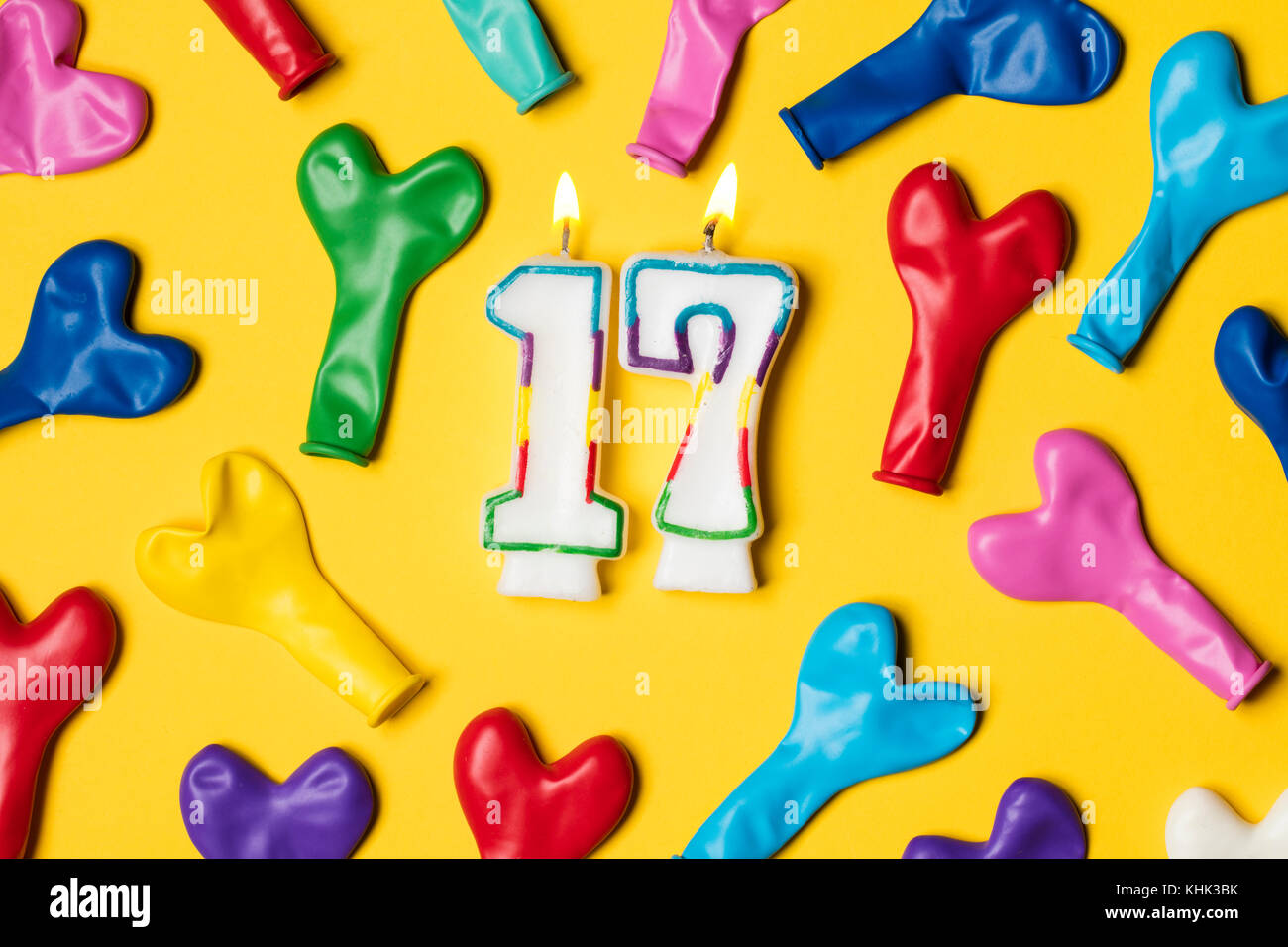 Number 17 candle with party balloons on a bright yellow background ...