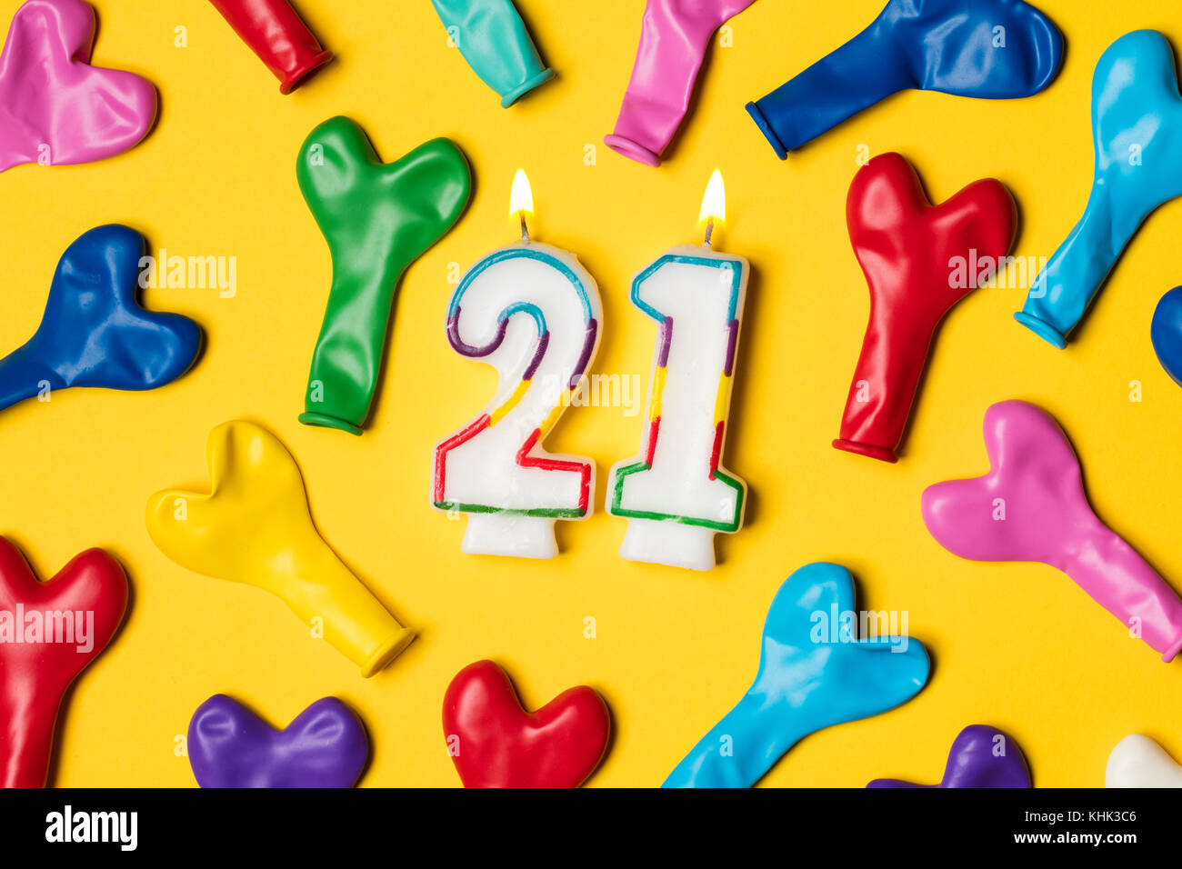 Number 21 candle with party balloons on a bright yellow background ...