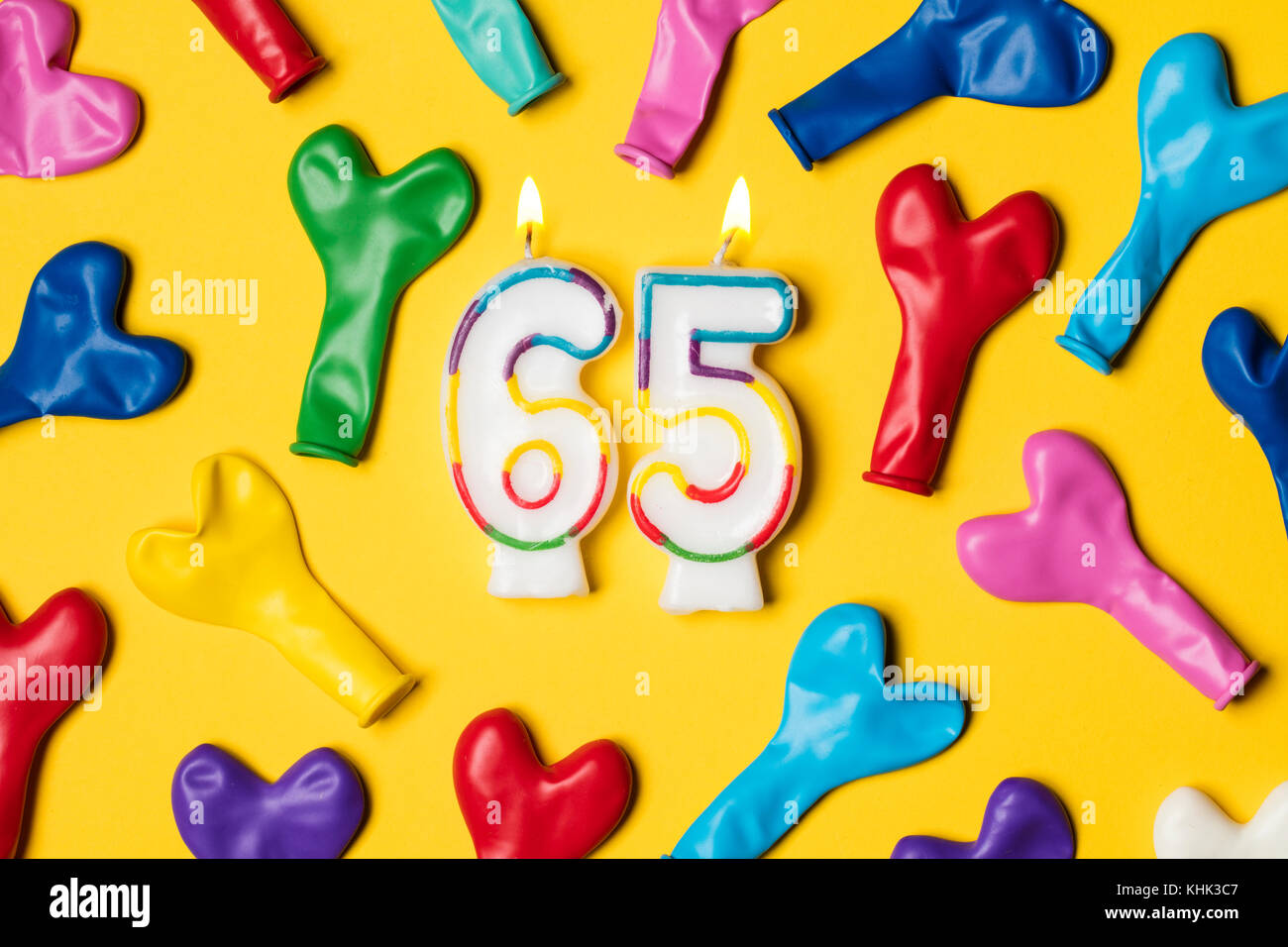 Number 65 candle with party balloons on a bright yellow background ...