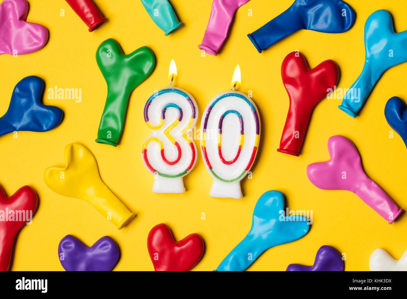Number 30 candle with party balloons on a bright yellow background ...
