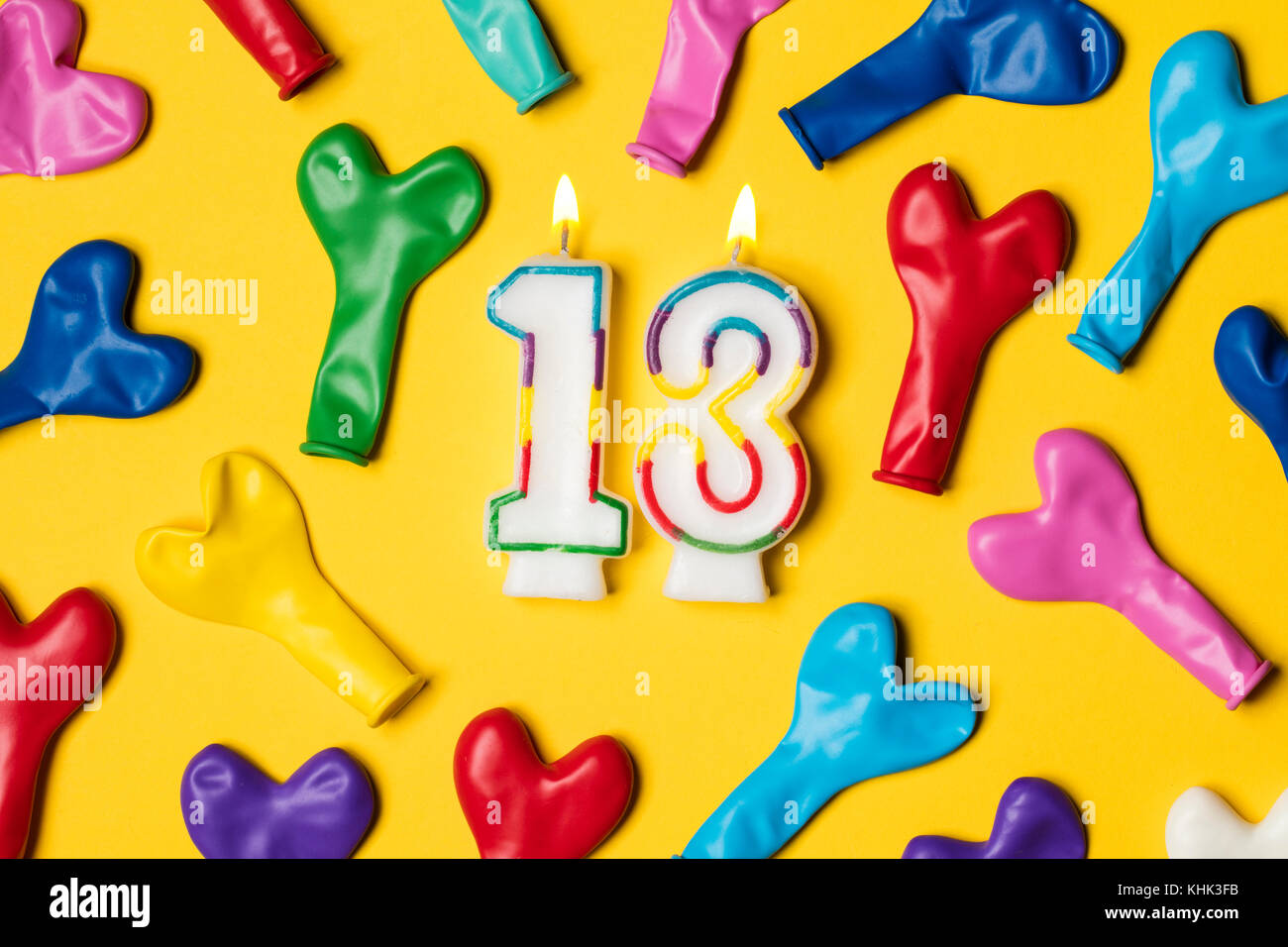 Number 13 candle with party balloons on a bright yellow background ...