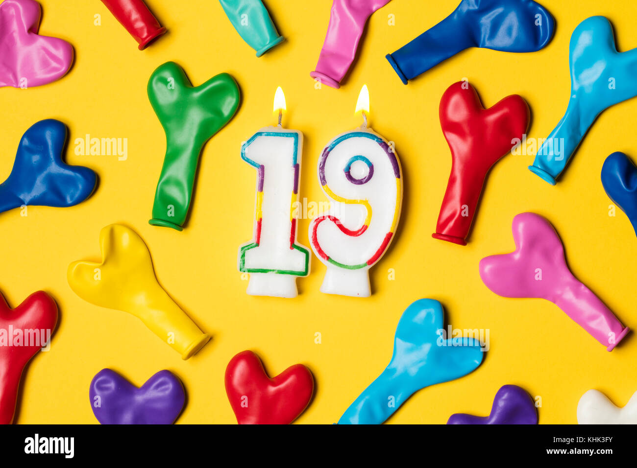 Number 19 candle with party balloons on a bright yellow background ...