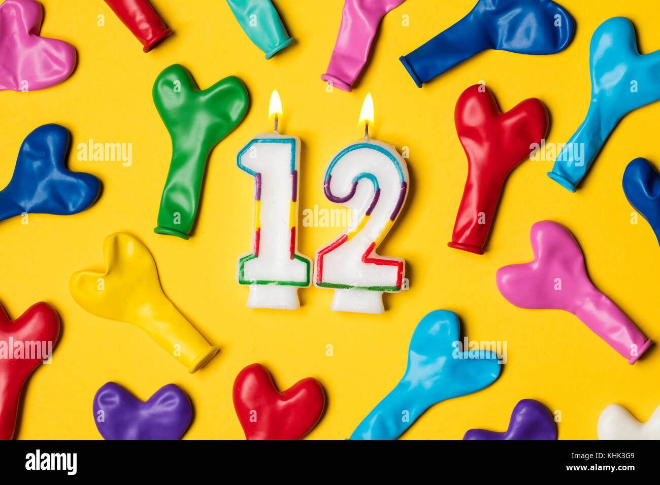 Number 12 candle with party balloons on a bright yellow background ...