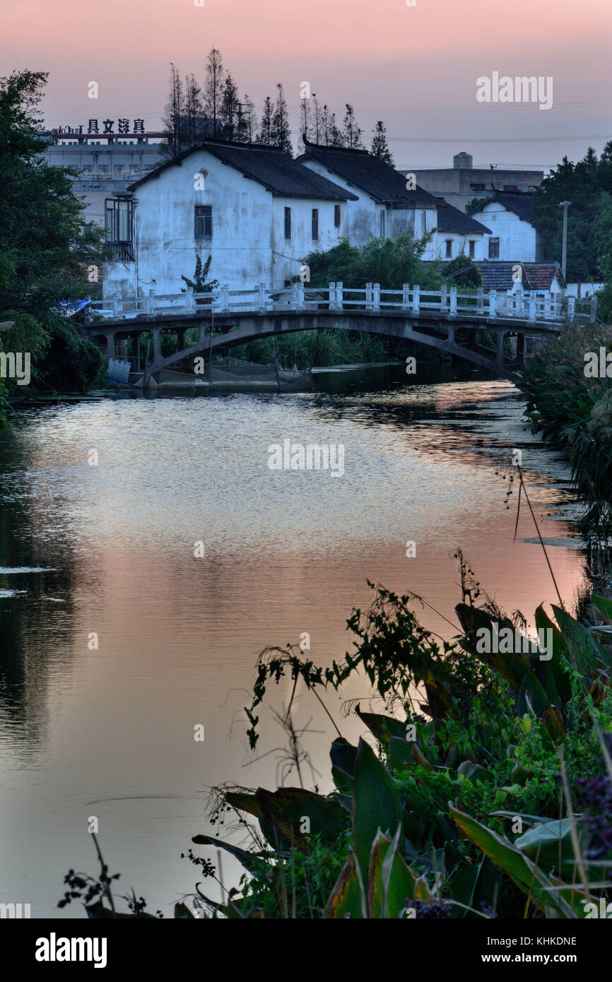 Traditional house next to stream reflecting sunset colors on the water ...