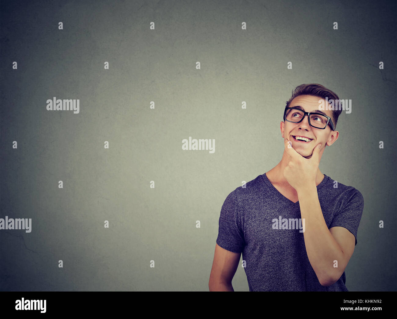 Handsome thoughtful young man making up his mind looking up smiling ...