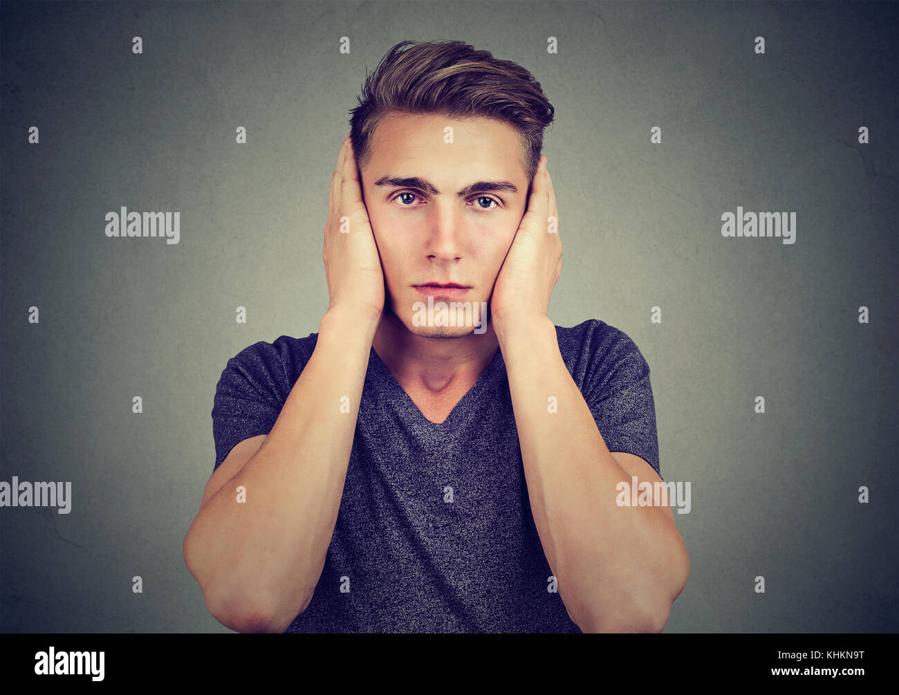 Portrait of a tranquil relaxed man covering his ears looking at camera ...