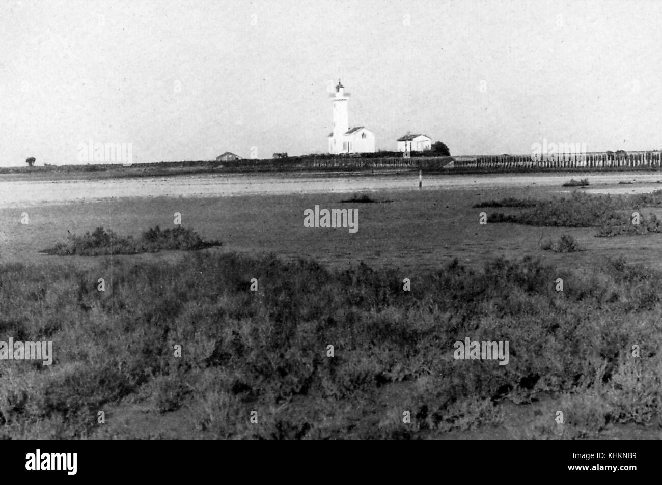 A photograph of a lighthouse from a distance, several shorter buildings ...