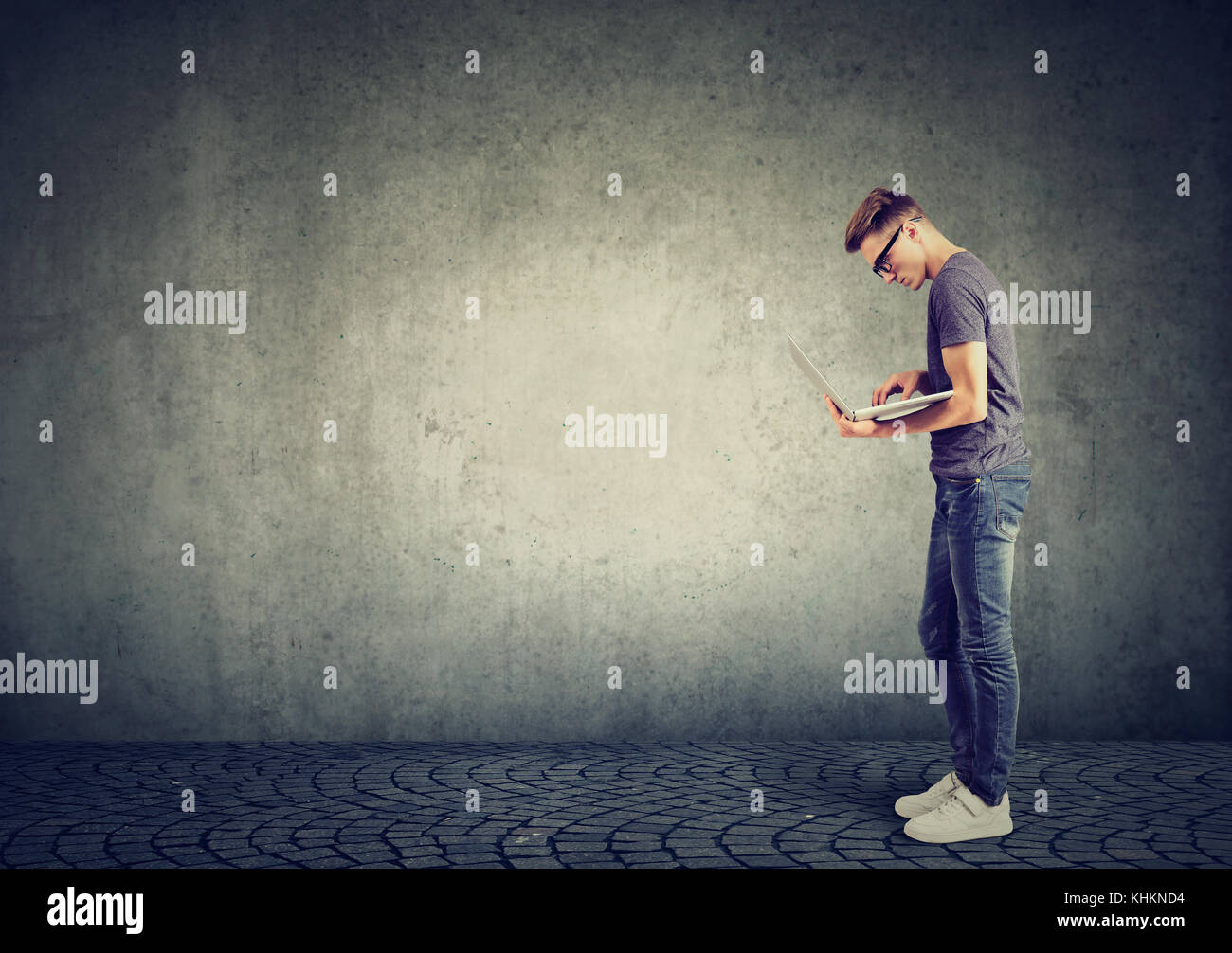 Portrait of young man standing using his laptop computer Stock Photo ...