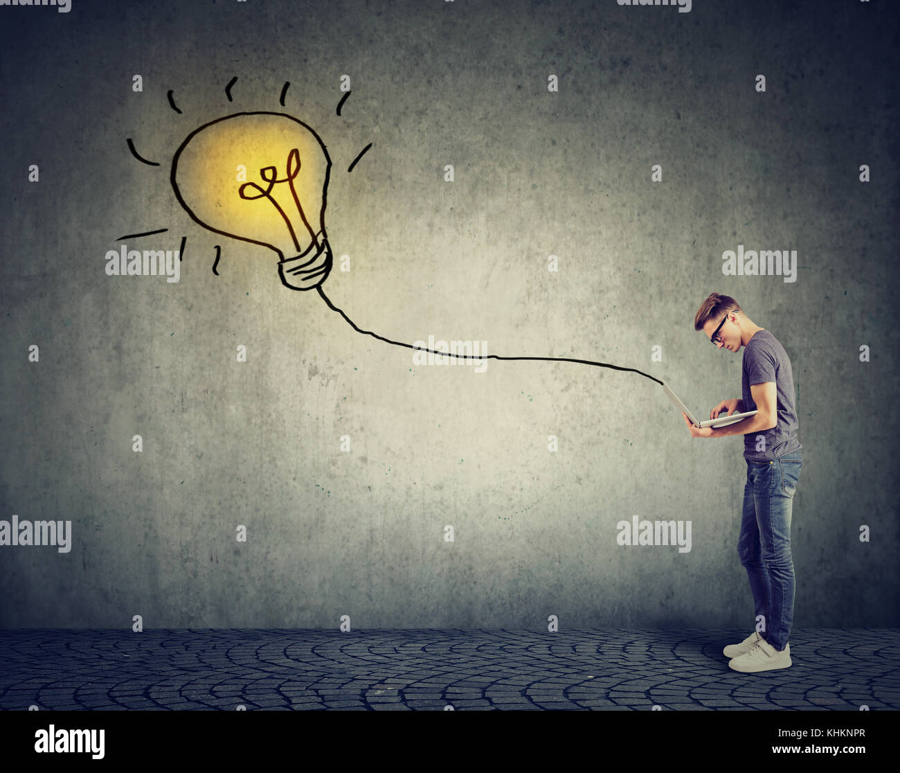 Young man using a laptop with light bulb plugged in it Stock Photo - Alamy