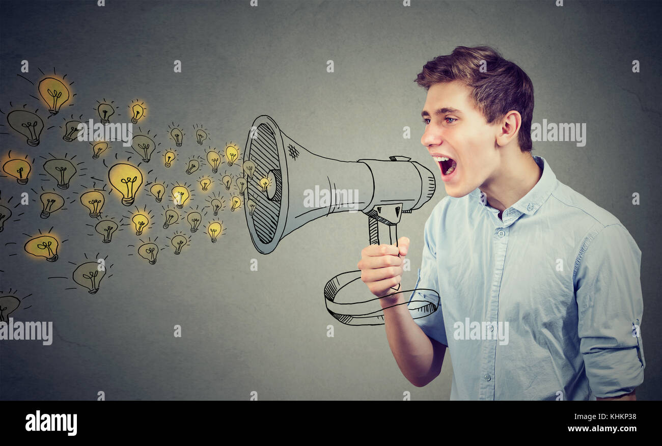 Man screaming out his ideas loud in megaphone isolated on gray wall ...