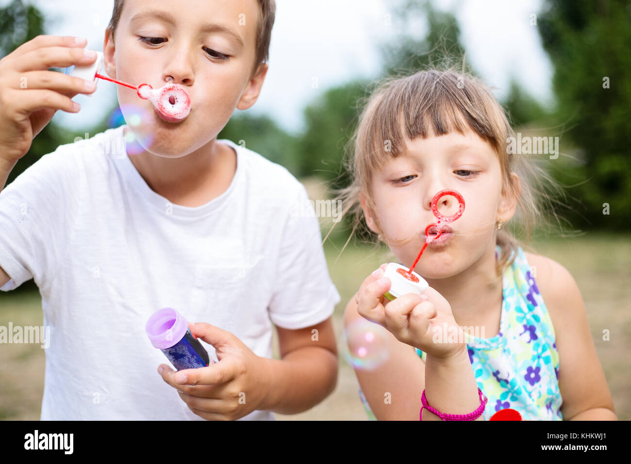 Close-up portrait of two eastern european small children blowing bubbles outdoors in park on ...