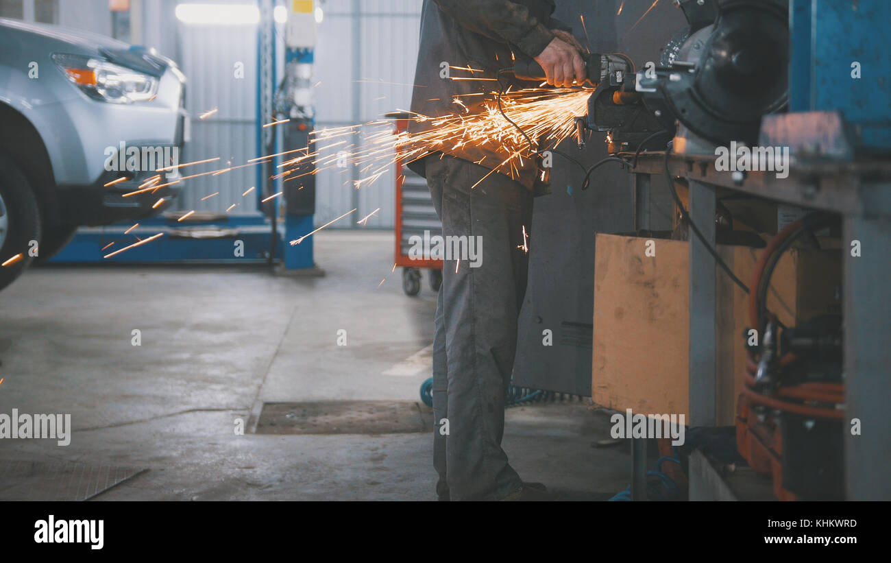 Car auto service - worker grinding metal construction with a circular ...