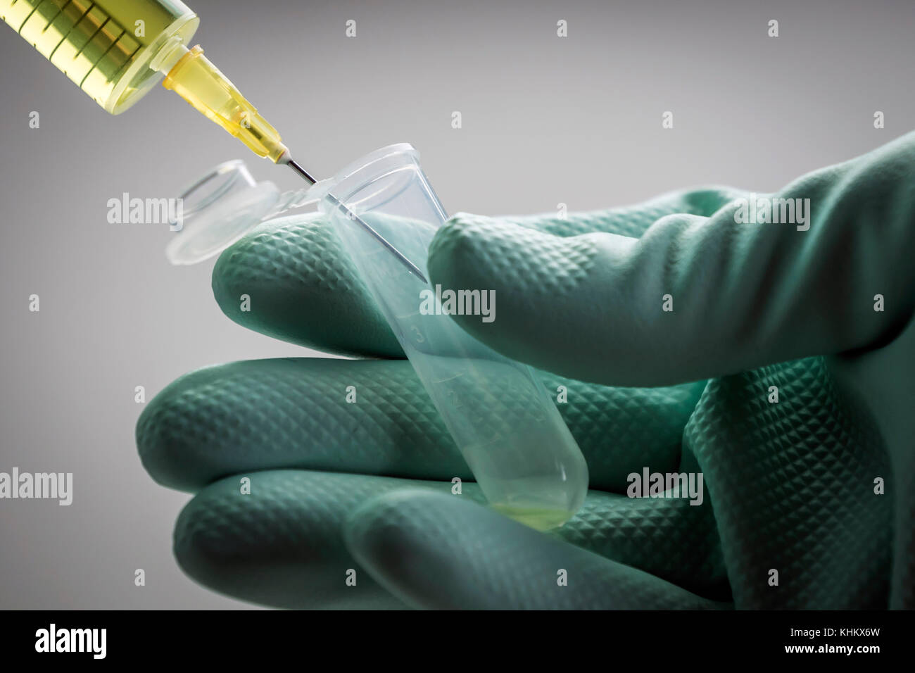 Scientist with green latex gloves manipulates vial and syringe in ...