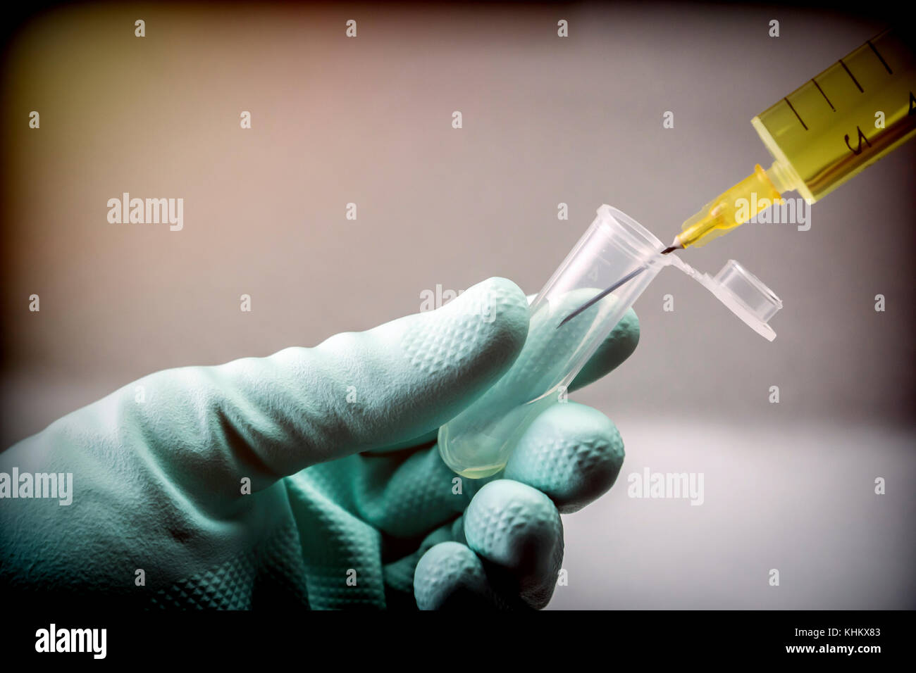 Scientist with green latex gloves manipulates vial and syringe in ...